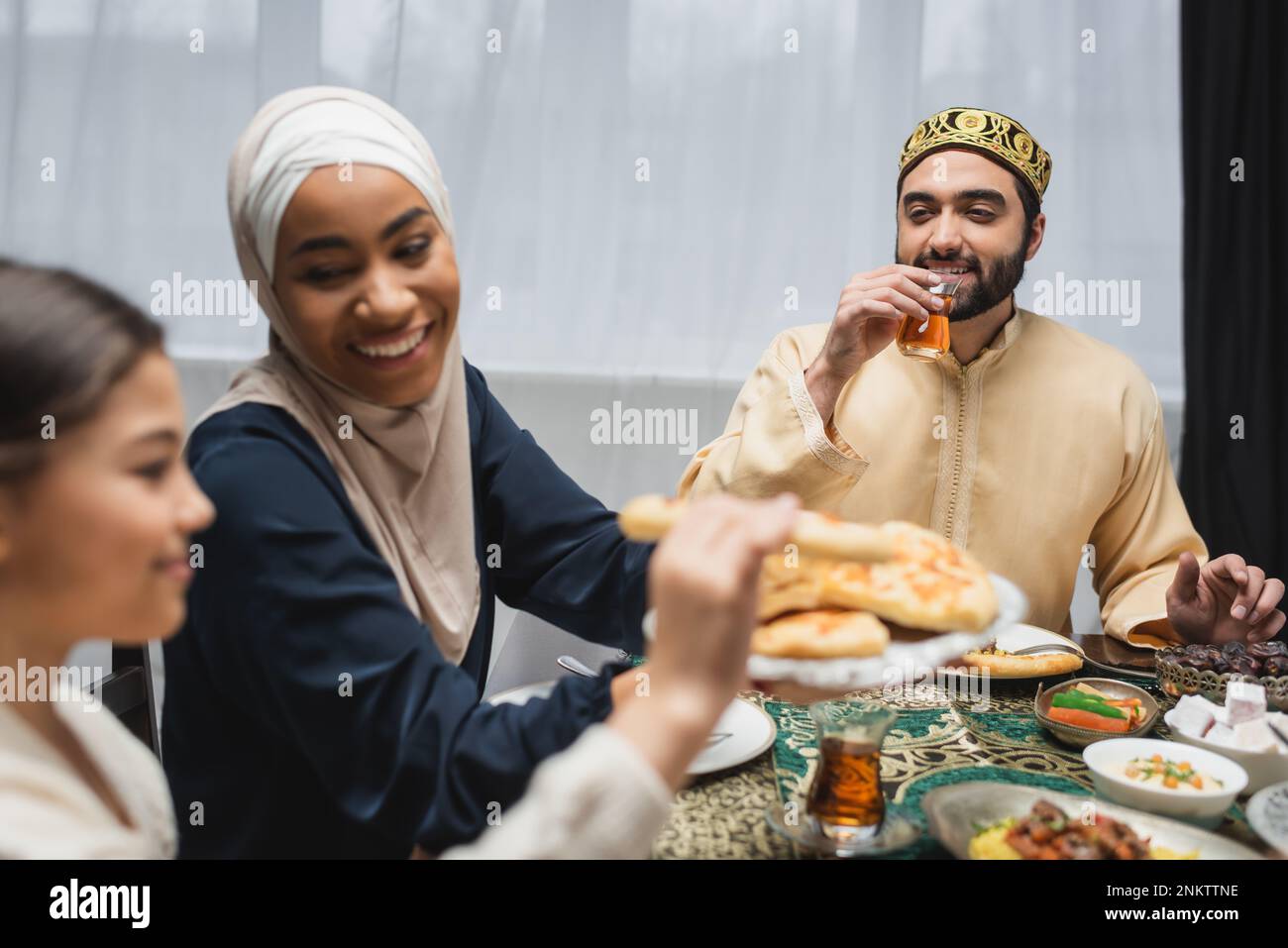 Smiling muslim man holding turkish tea glass near family and ramadan ...