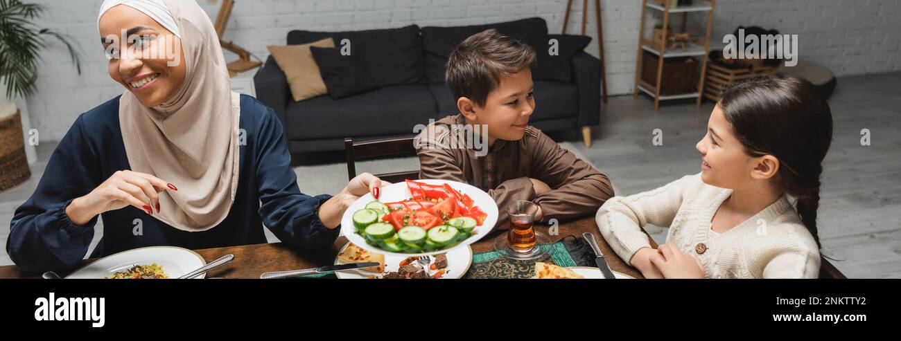 Smiling african american mother holding food near kids during iftar at ...