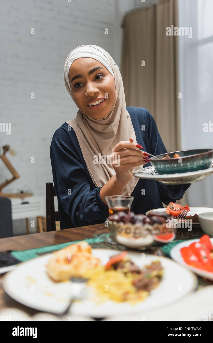 Smiling african american woman in hijab holding food during iftar at ...