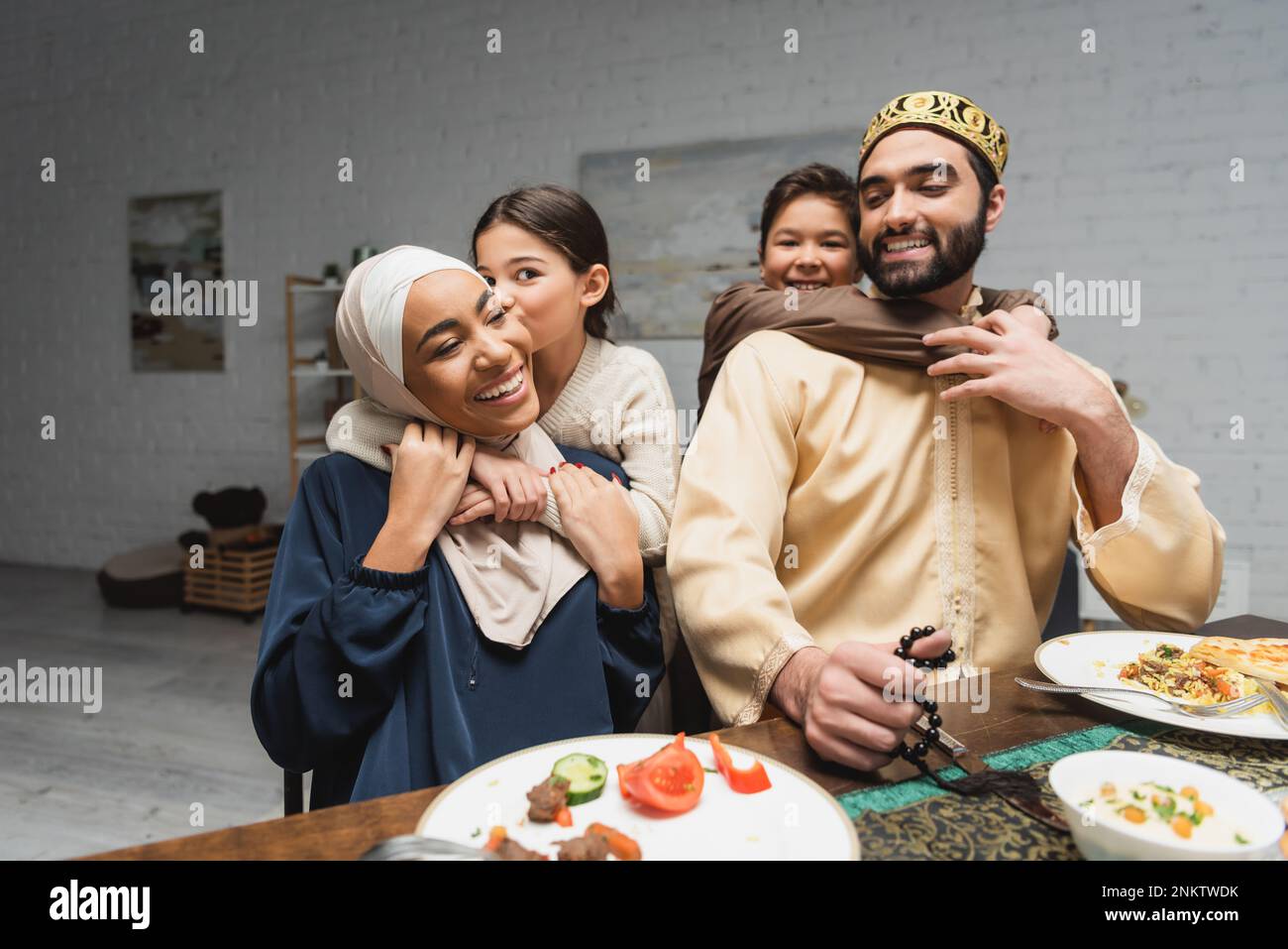 Smiling muslim children hugging parents during ramadan dinner at home ...