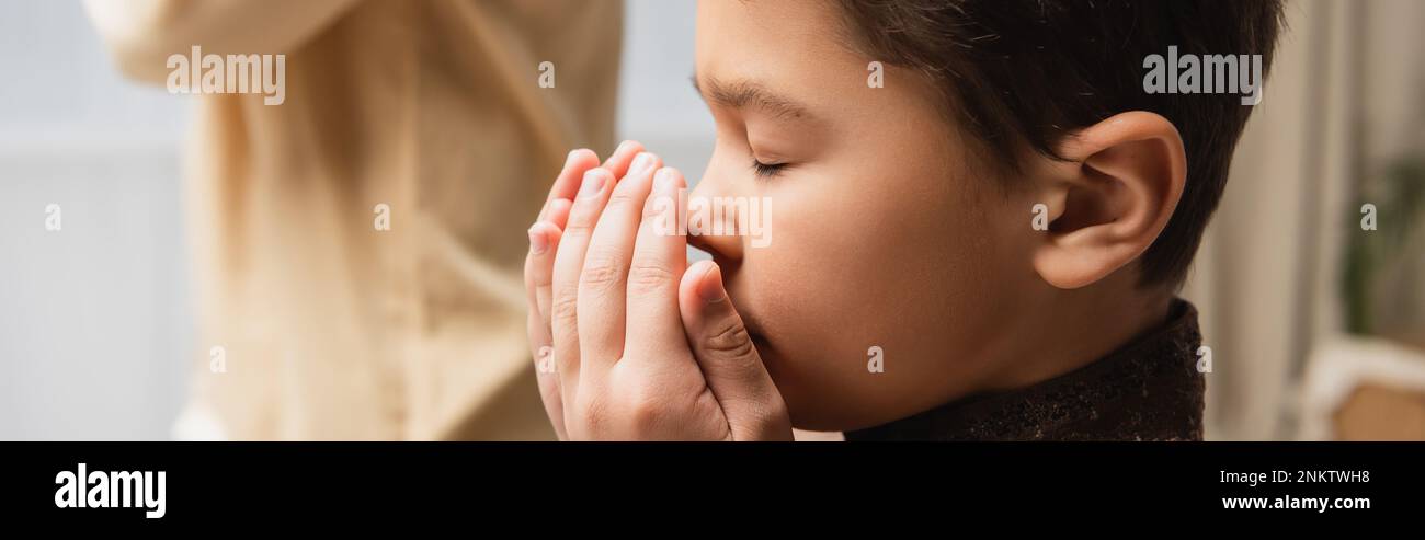 Muslim child praying near blurred parent during salah at home, banner ...