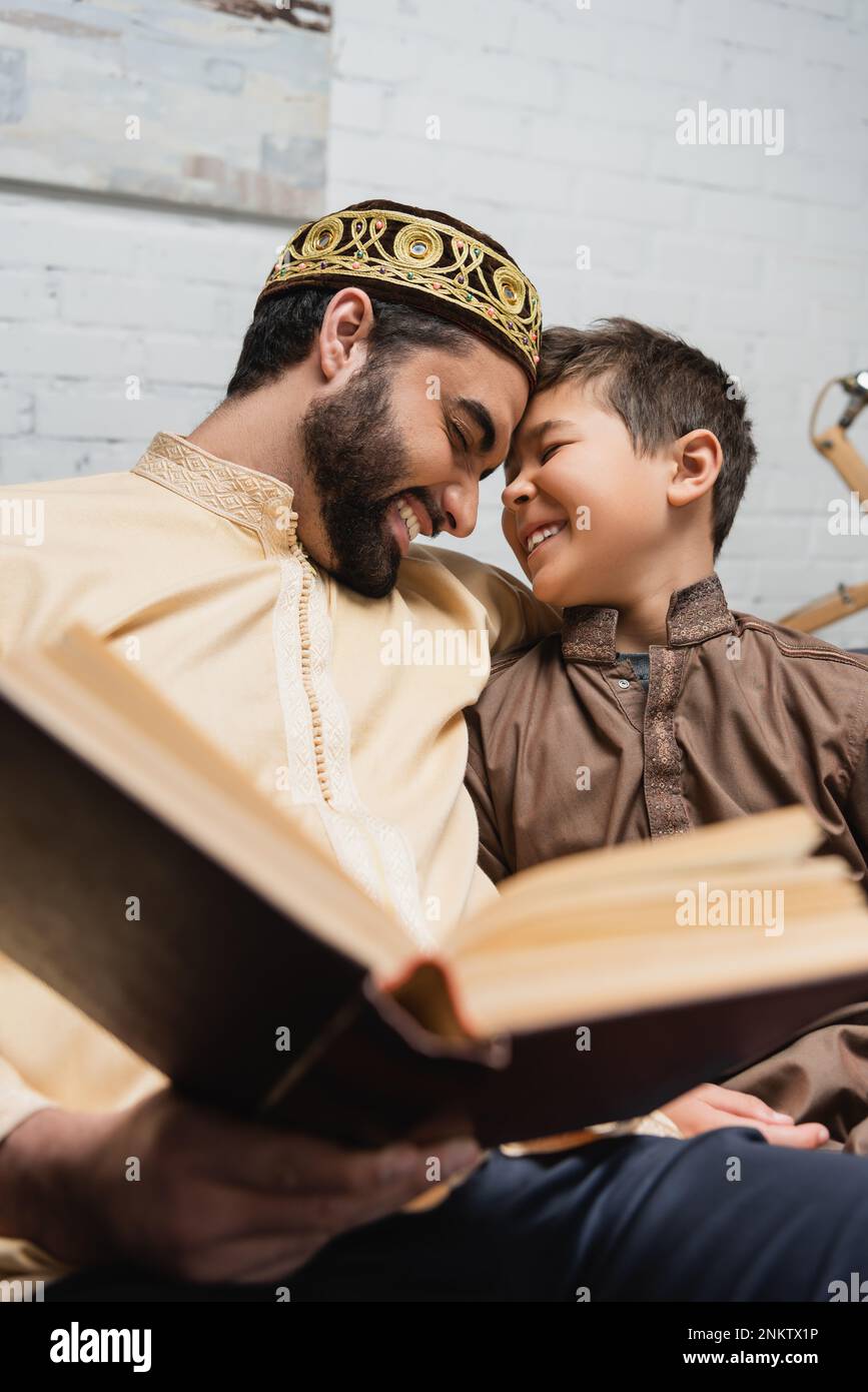 Cheerful middle eastern man and son reading blurred book at home,stock ...
