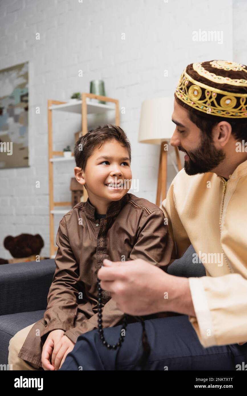 Smiling muslim boy looking at father with prayer beads at home,stock ...