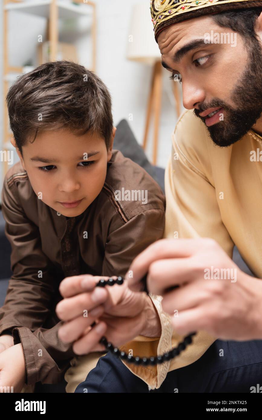 Middle eastern man holding blurred prayer beads and talking to son at ...