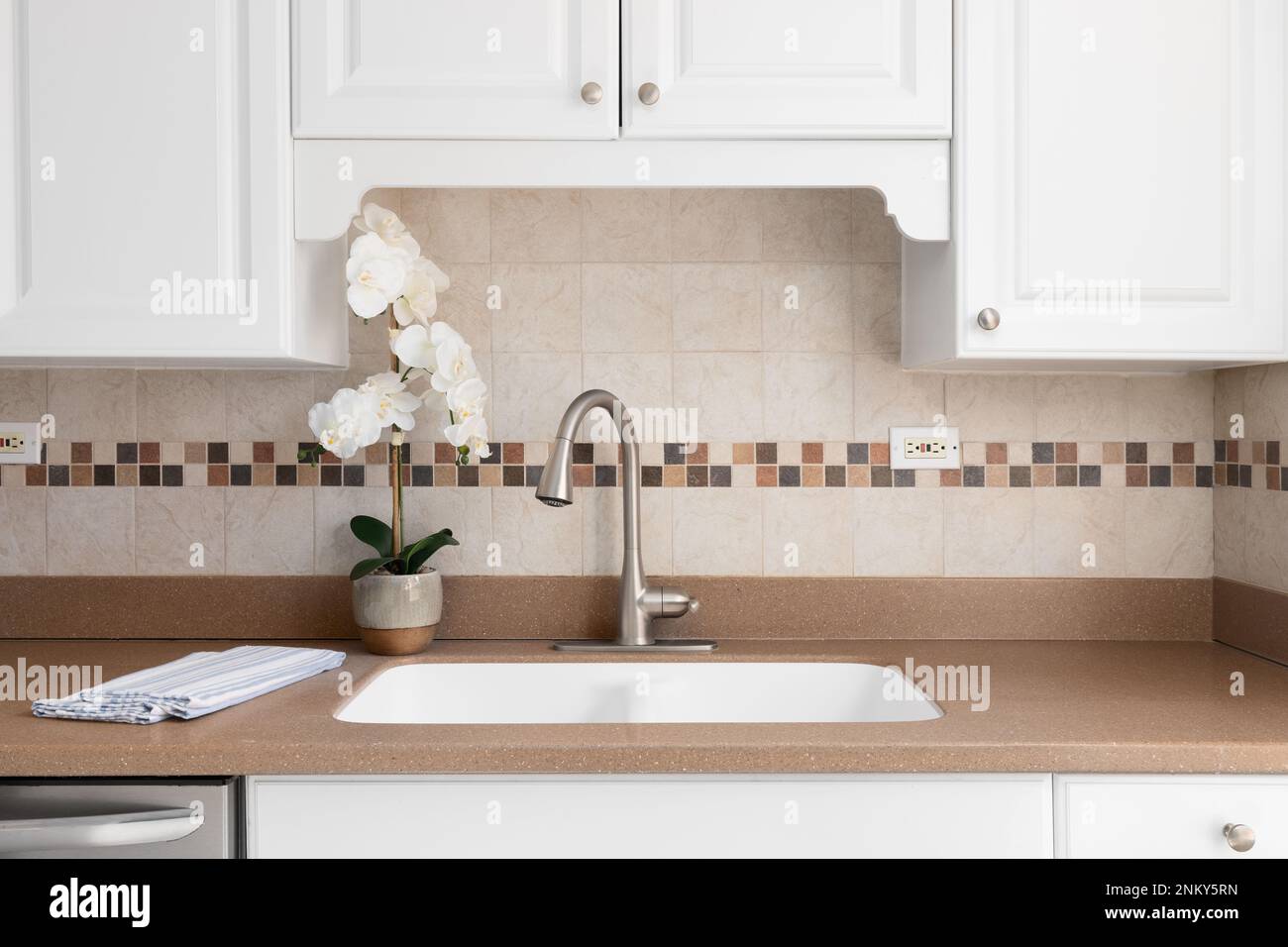 A kitchen faucet sink detail with white cabinets, brown countertop, and ...