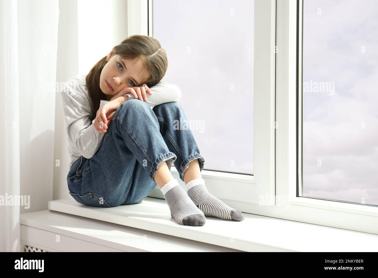 Sad little girl sitting on window sill indoors, space for text Stock ...