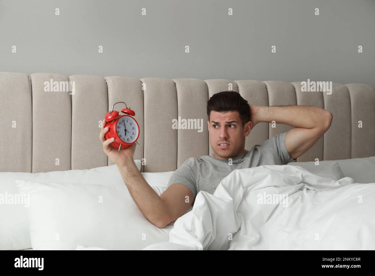 Emotional man with alarm clock in bed. Being late because of ...