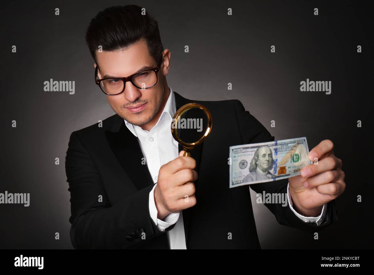 Expert authenticating 100 dollar banknote with magnifying glass against ...