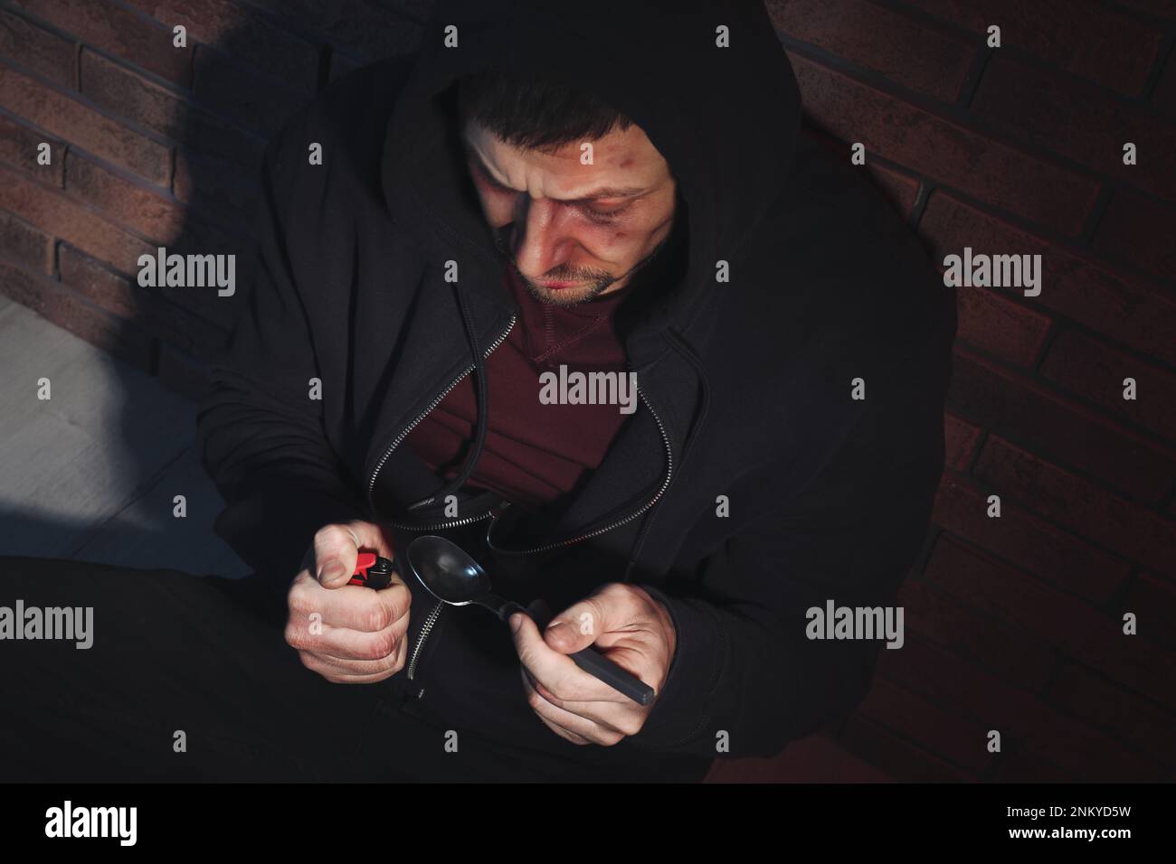 Man preparing drug with spoon and lighter near brick wall Stock Photo ...