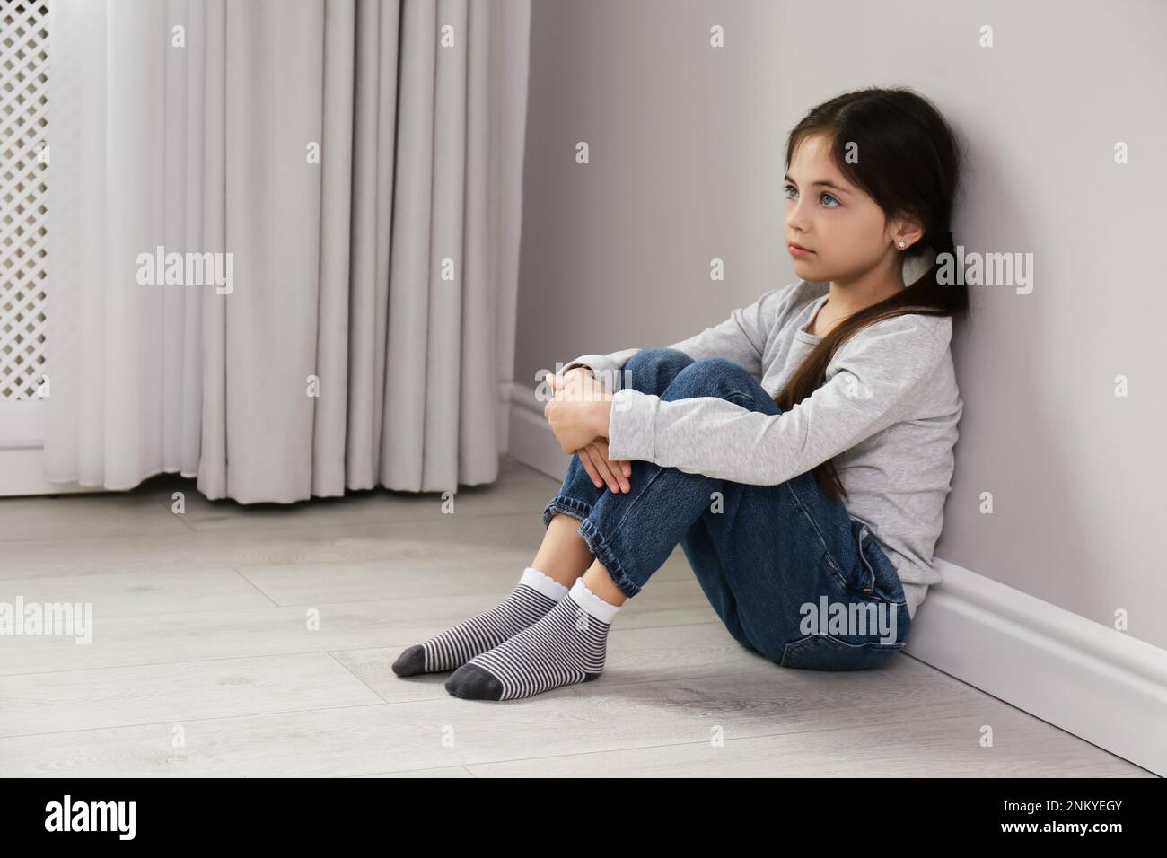 Sad little girl sitting on floor indoors, space for text Stock Photo ...