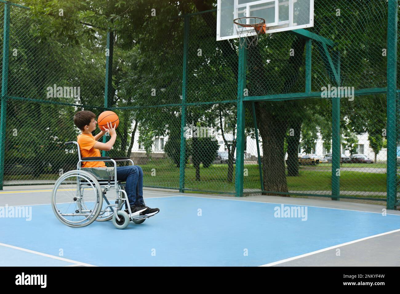 Disabled teenage boy in wheelchair playing basketball on outdoor court ...