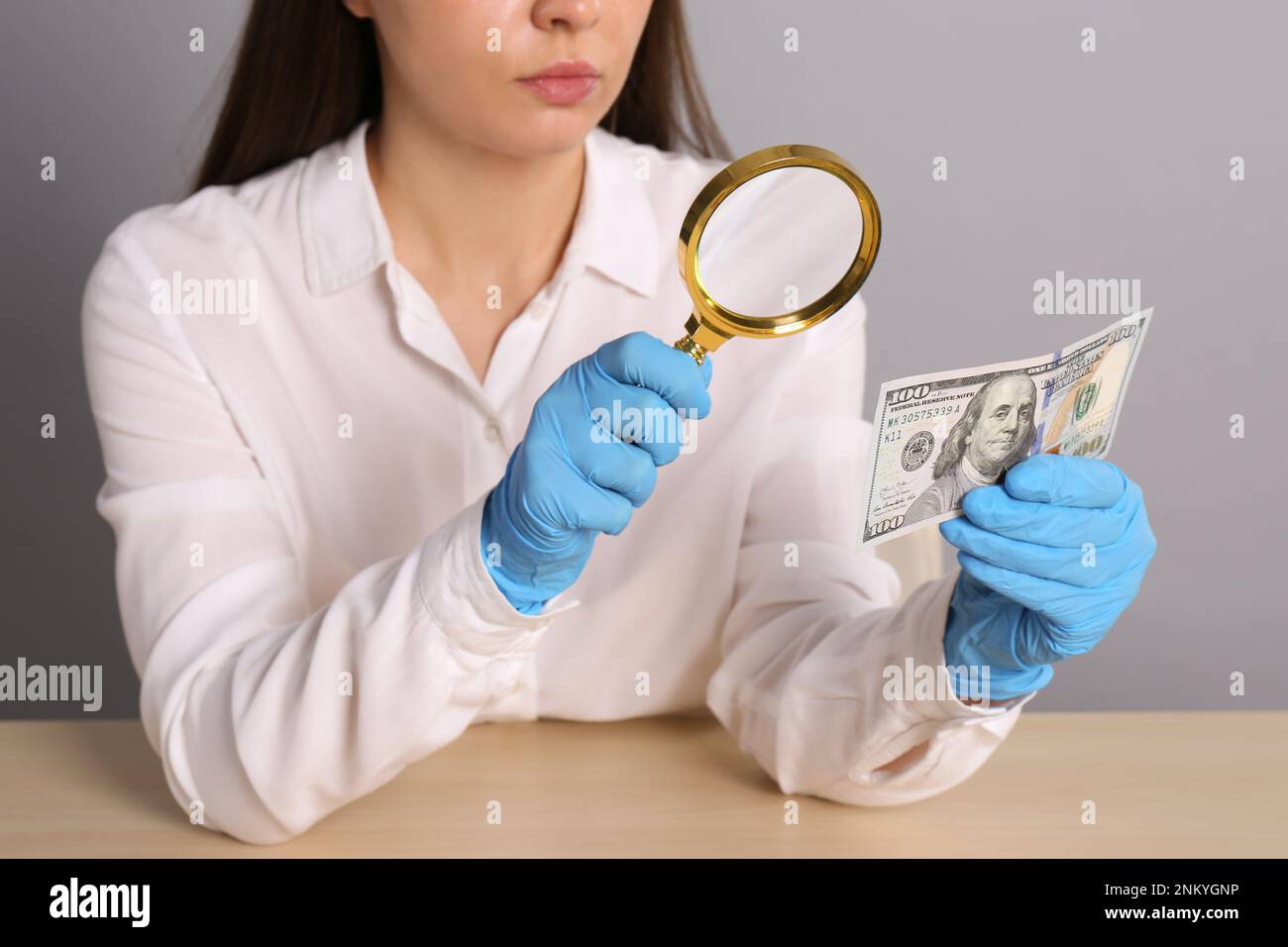 Expert authenticating 100 dollar banknote with magnifying glass at ...