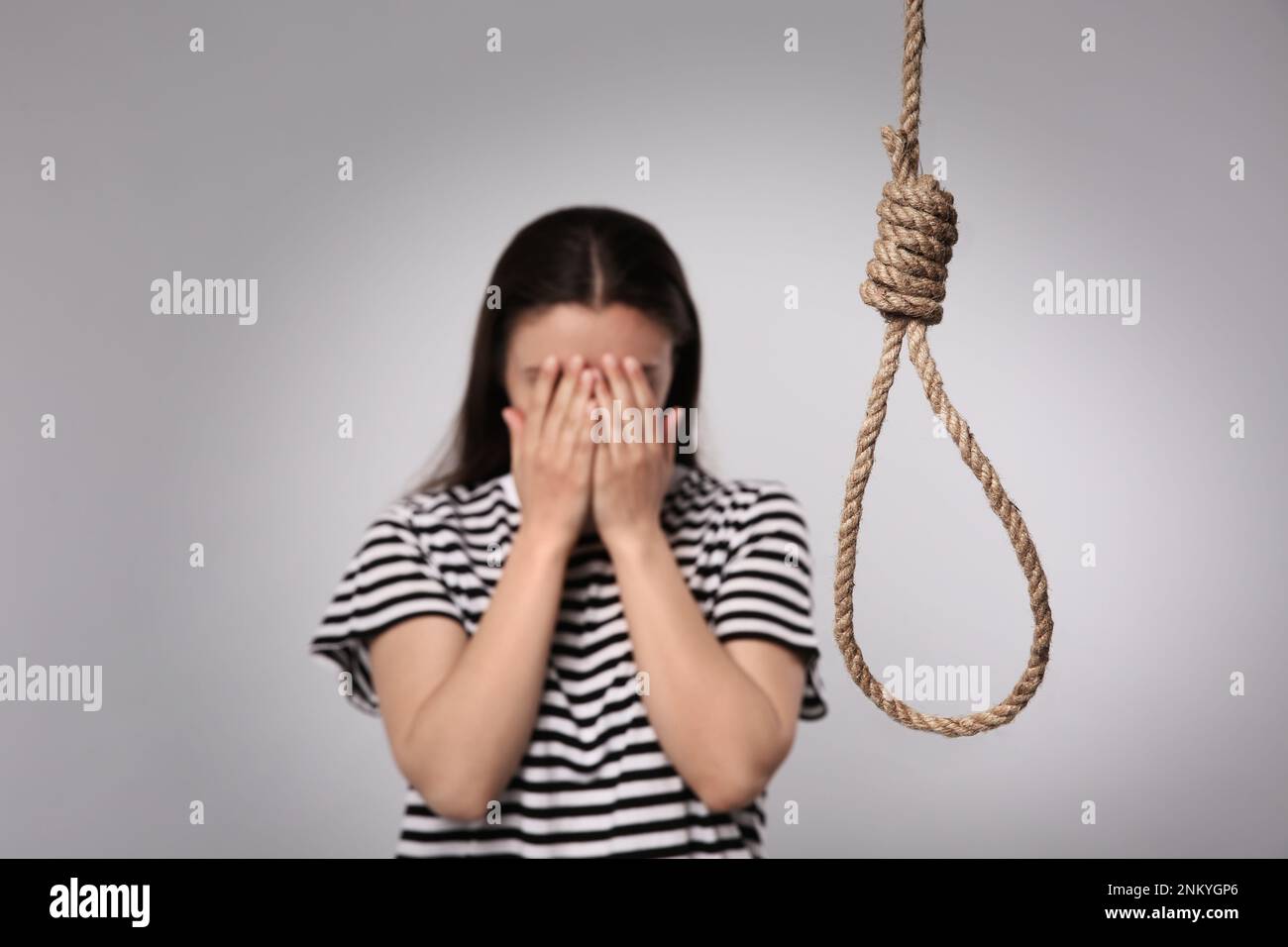 Depressed woman crying near rope noose on light grey background Stock ...