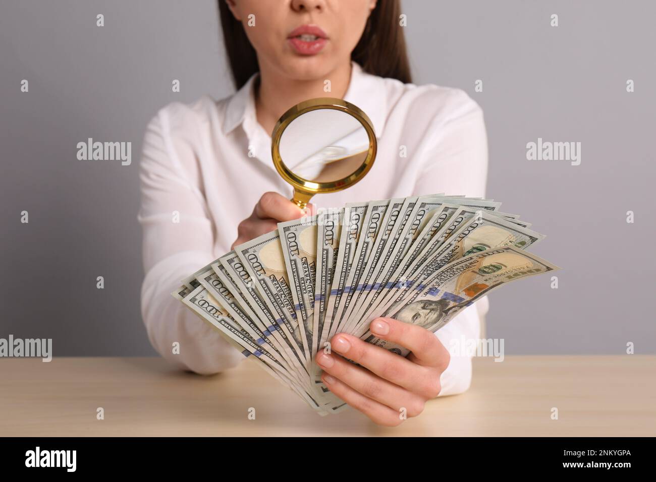 Expert authenticating 100 dollar banknotes with magnifying glass at ...