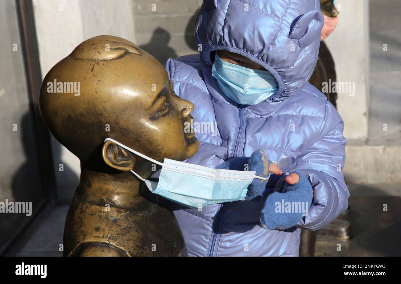 A child puts a face mask on a statue face in Beijing on Jan. 31, 2022 ...