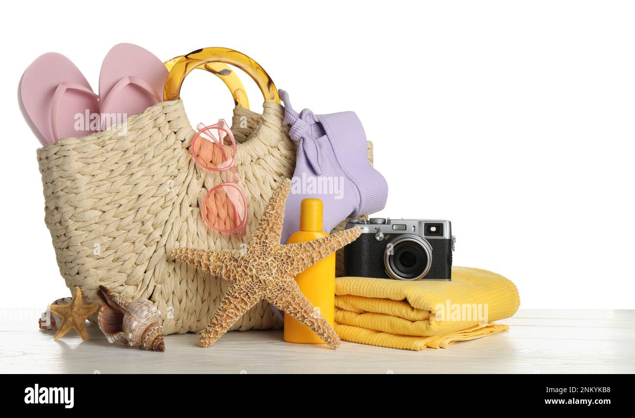 Bag with different beach objects on wooden table against white ...