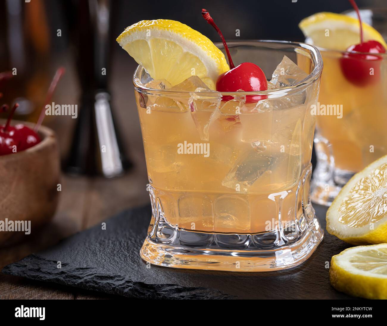 Whiskey sour cocktail with marachino cherry and lemon slice on black ...