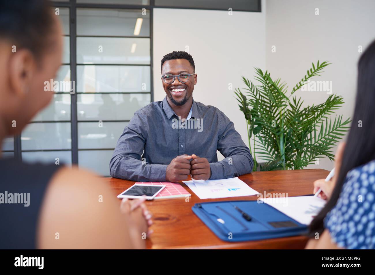 Three business colleagues sit around conference table, meeting smile ...