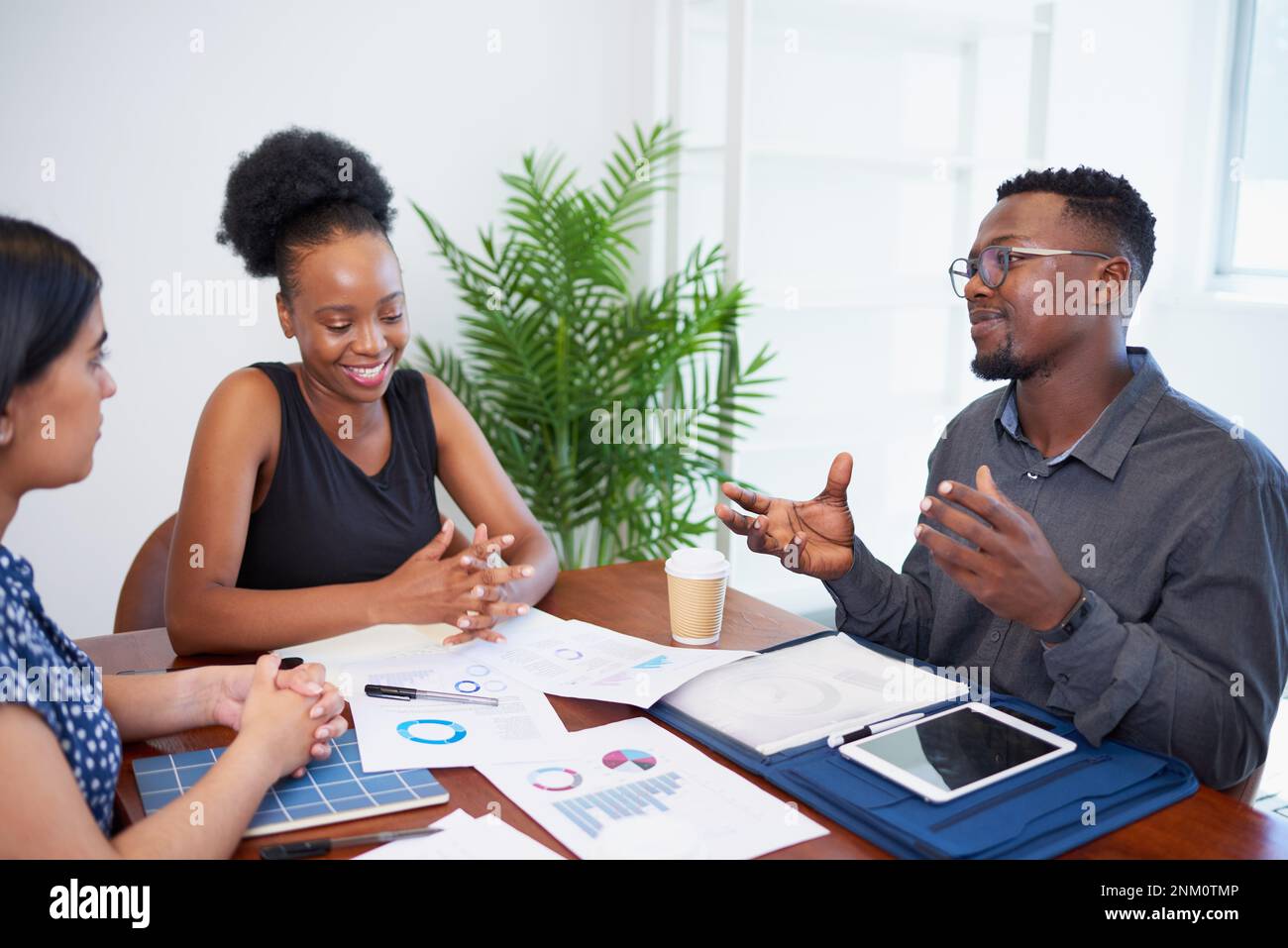 Three business colleagues discuss financial reports around boardroom ...