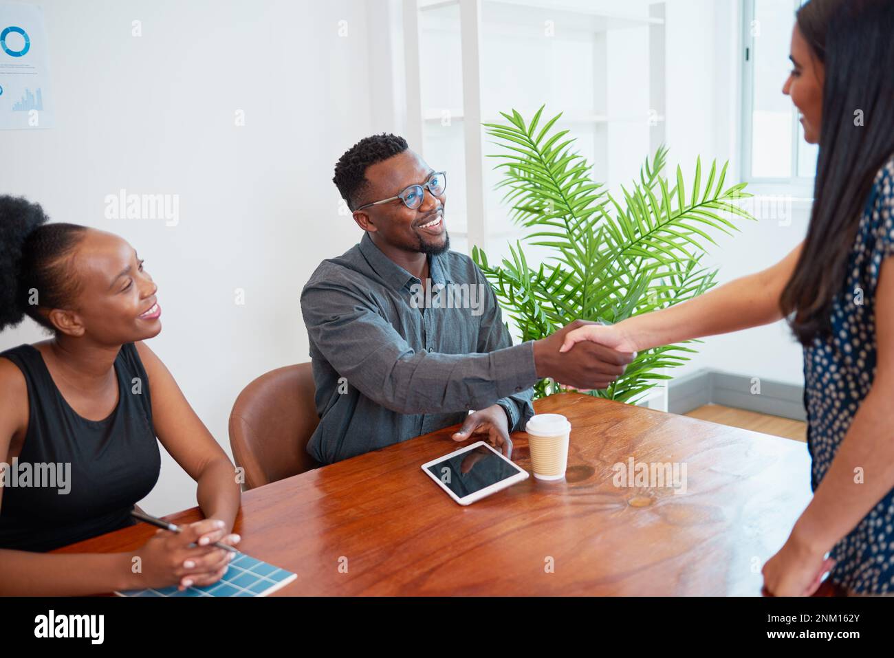 Business people shake hands around a conference table, greeting new ...