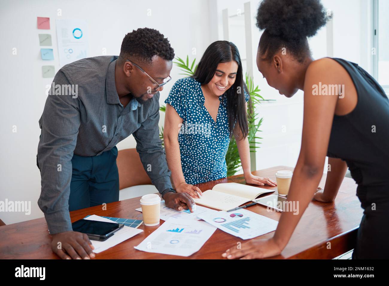 Three colleagues stand around conference table meeting about financial ...