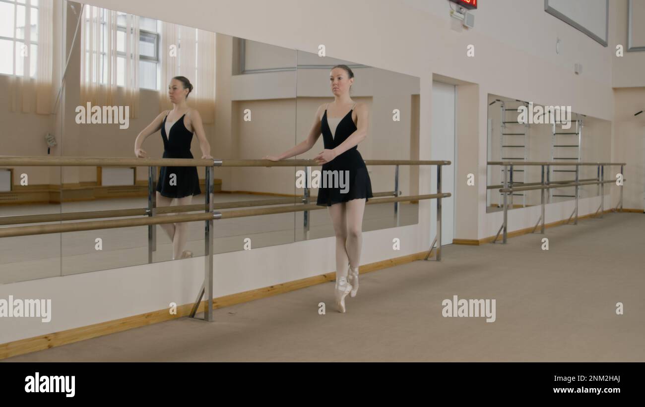 Ballerina in training bodysuit stands on tiptoe in front of ballet ...