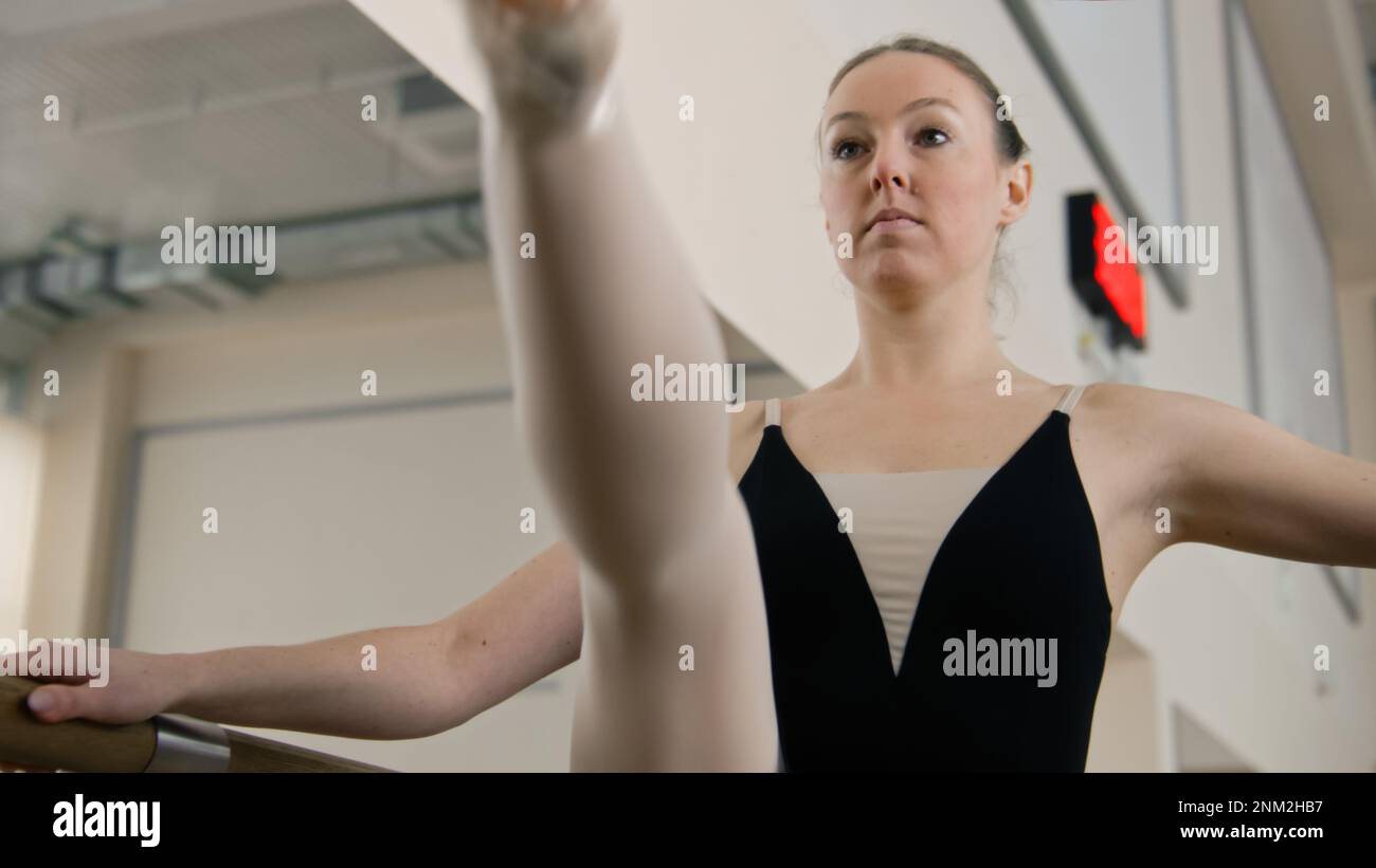 Ballerina in training bodysuit stands near ballet barre in dance studio ...