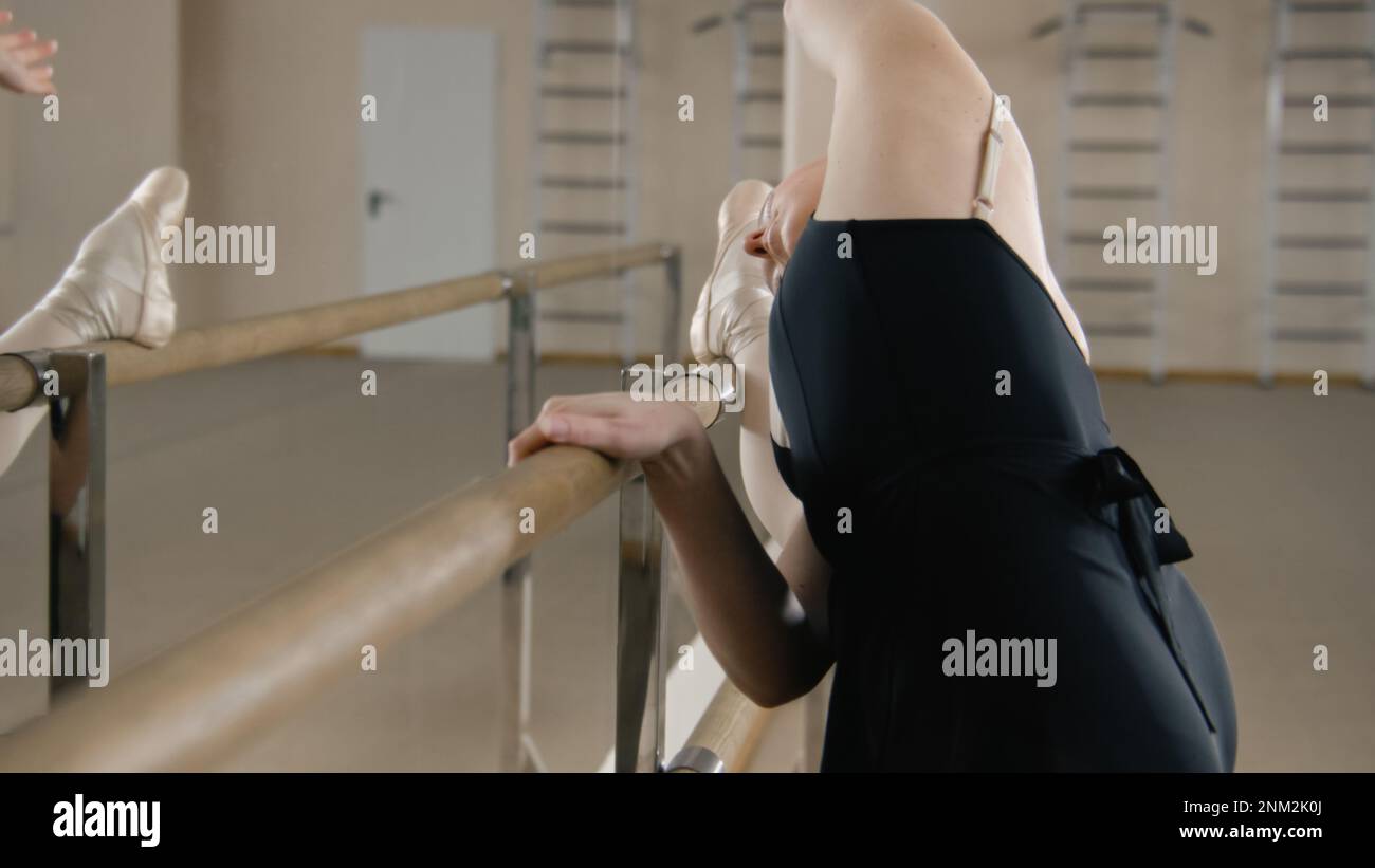 Graceful ballerina in training bodysuit stands near ballet barre ...