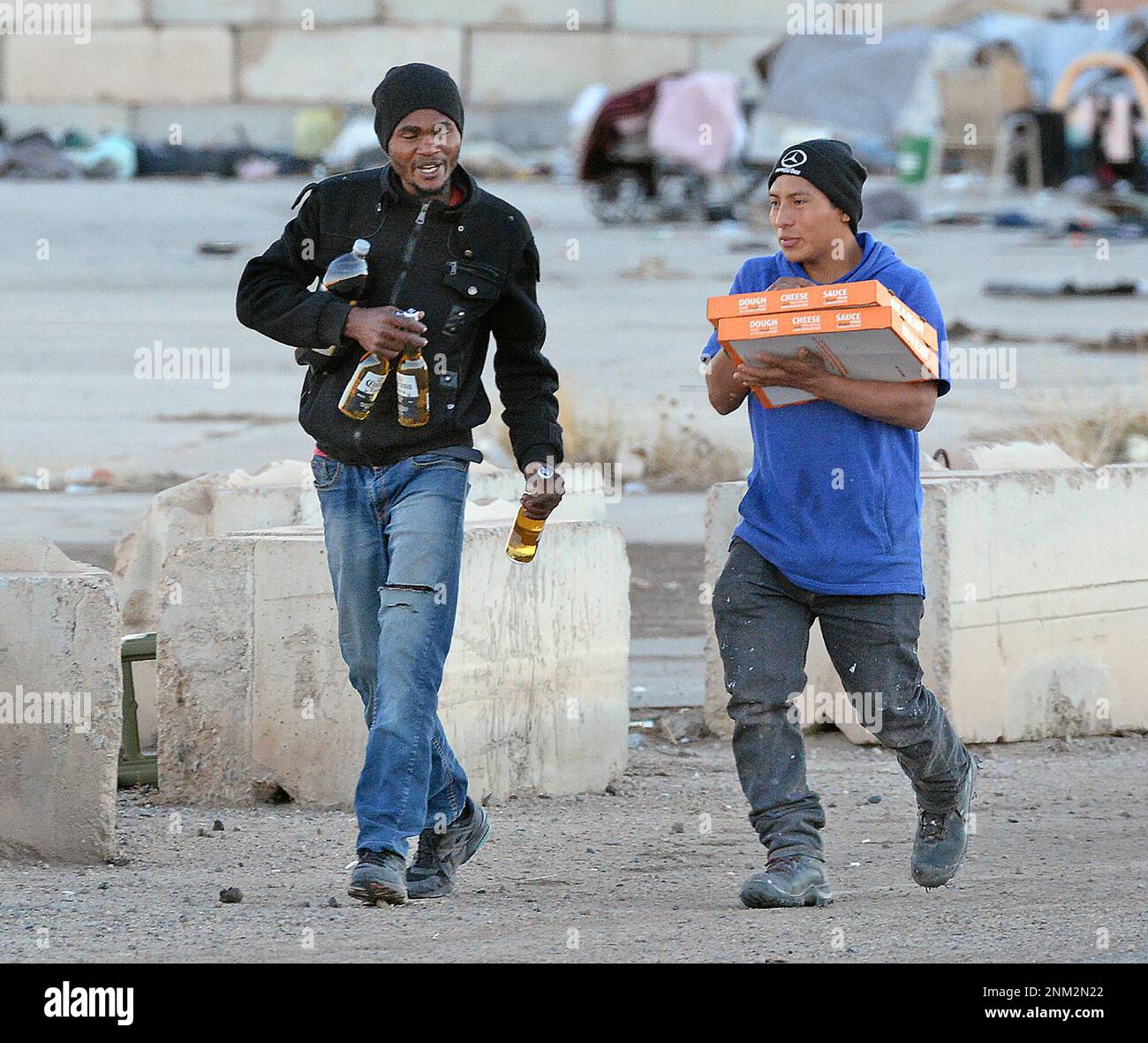 Two migrant men carry pizza and beverages to their makeshift living ...