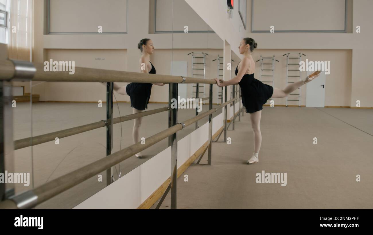 Ballerina in training bodysuit stands in front of ballet barre at dance ...