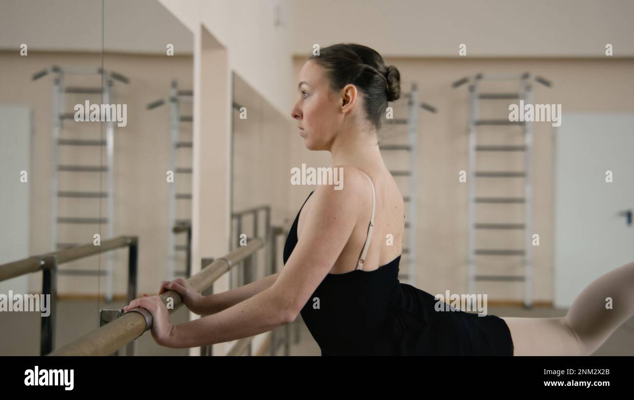 Ballet dancer in training bodysuit stands front of ballet barre in ...