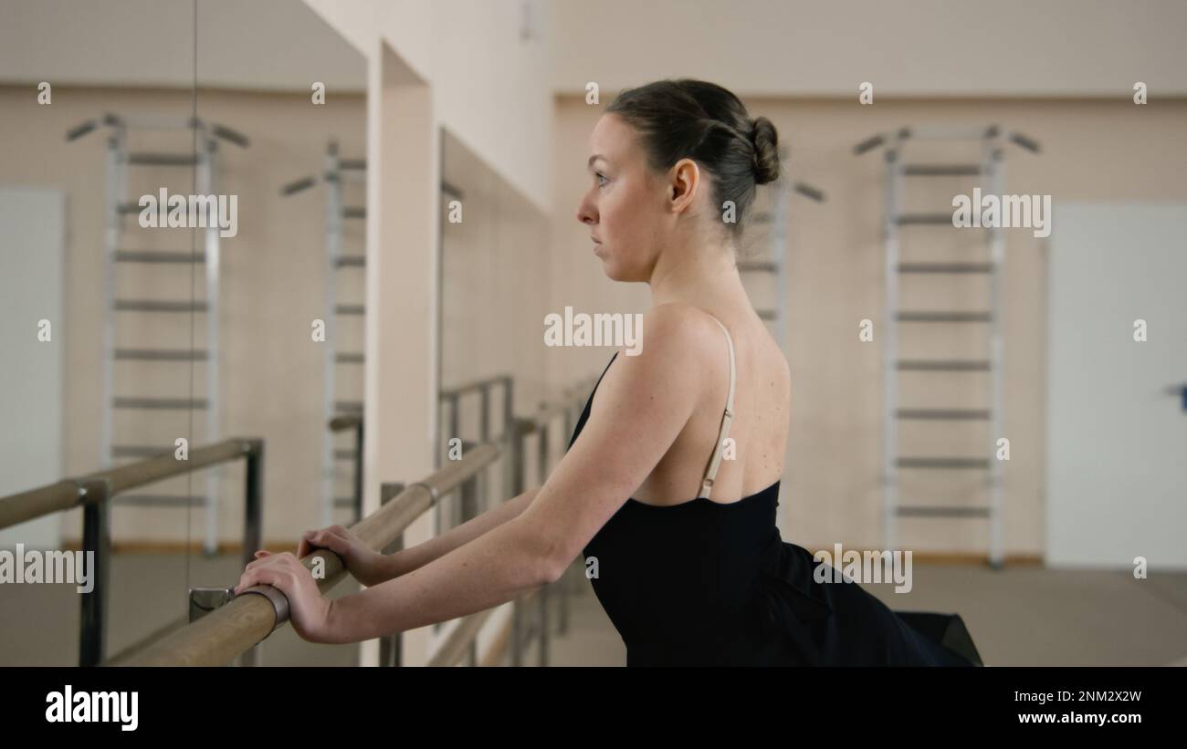 Ballet dancer in training bodysuit stands front of ballet barre in ...