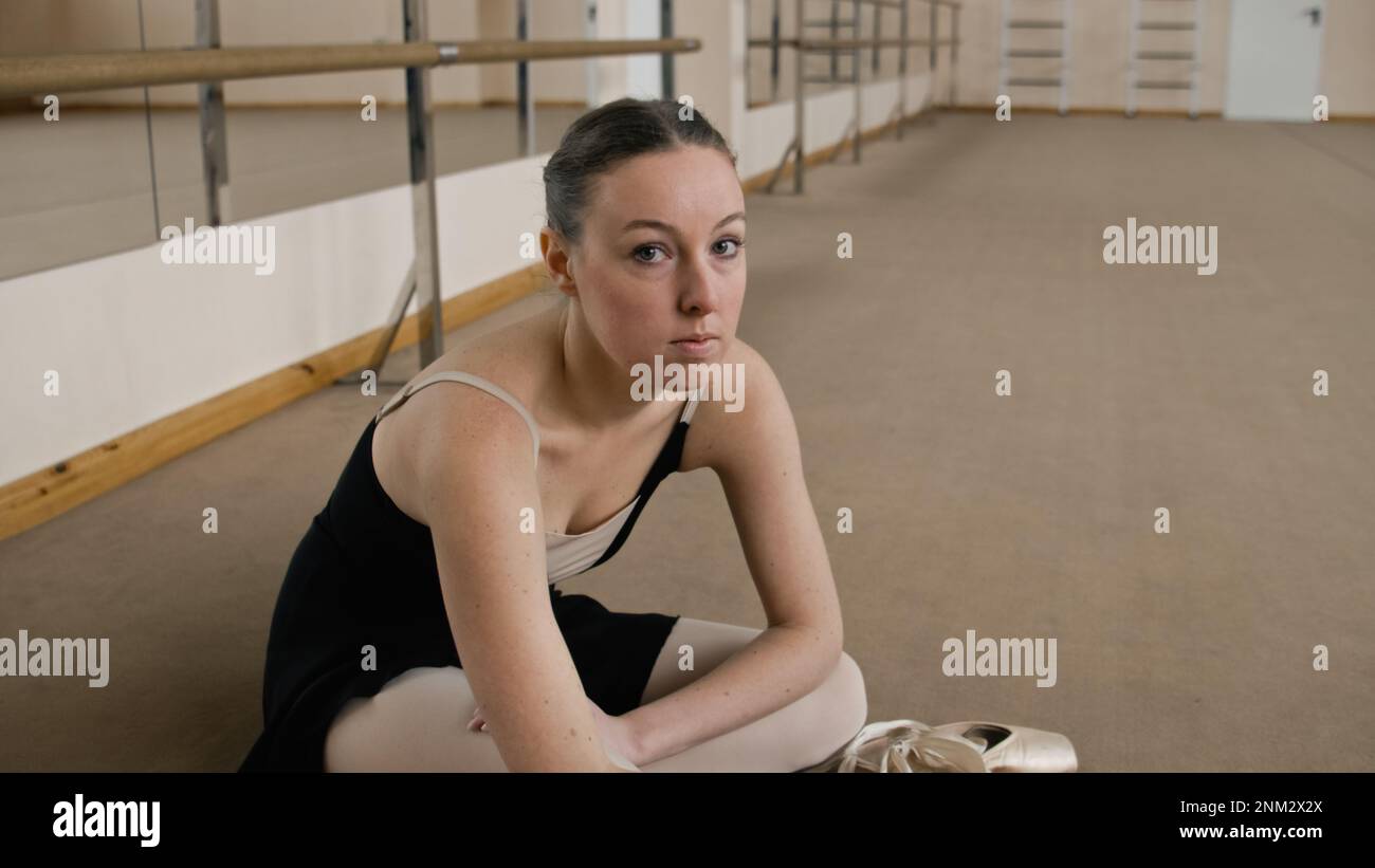 Tired ballerina in training bodysuit sits on the floor after stretching ...