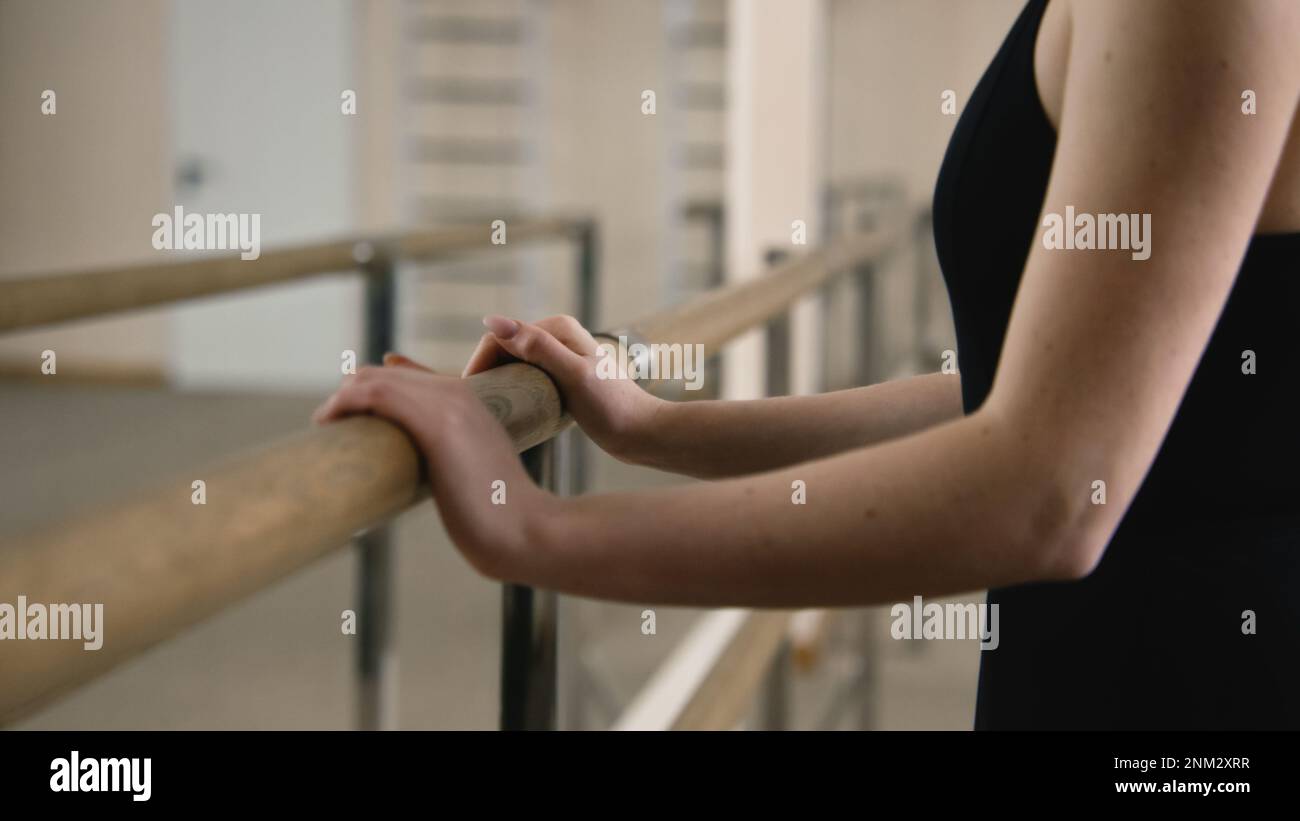 Ballerina in training bodysuit stands near ballet barre in dance studio ...