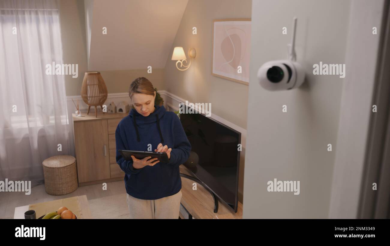 Caucasian woman installs security camera. Woman sets up angle of CCTV ...