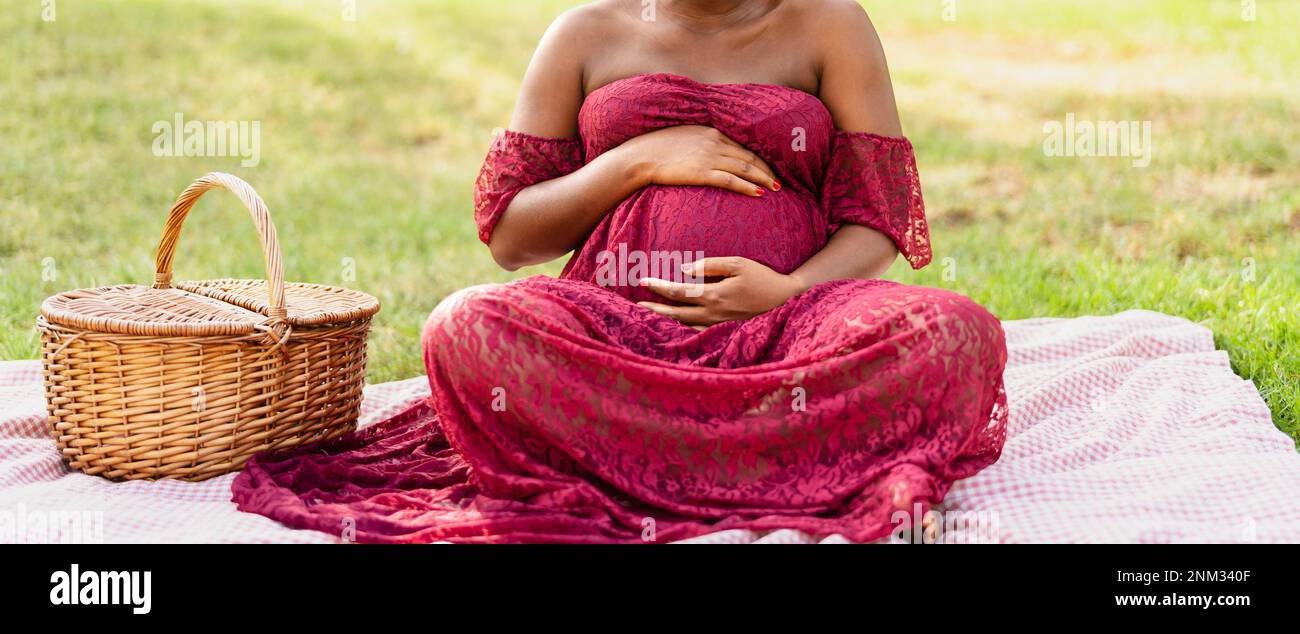 African woman caressing her pregnant belly while doing a picnic in park ...