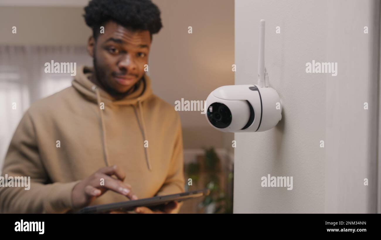 African American man installs security camera. Man sets up angle of ...