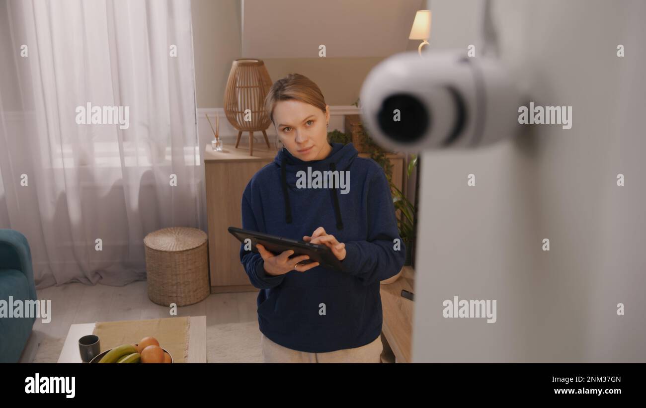 Caucasian woman installs security camera. Woman sets up angle of CCTV ...