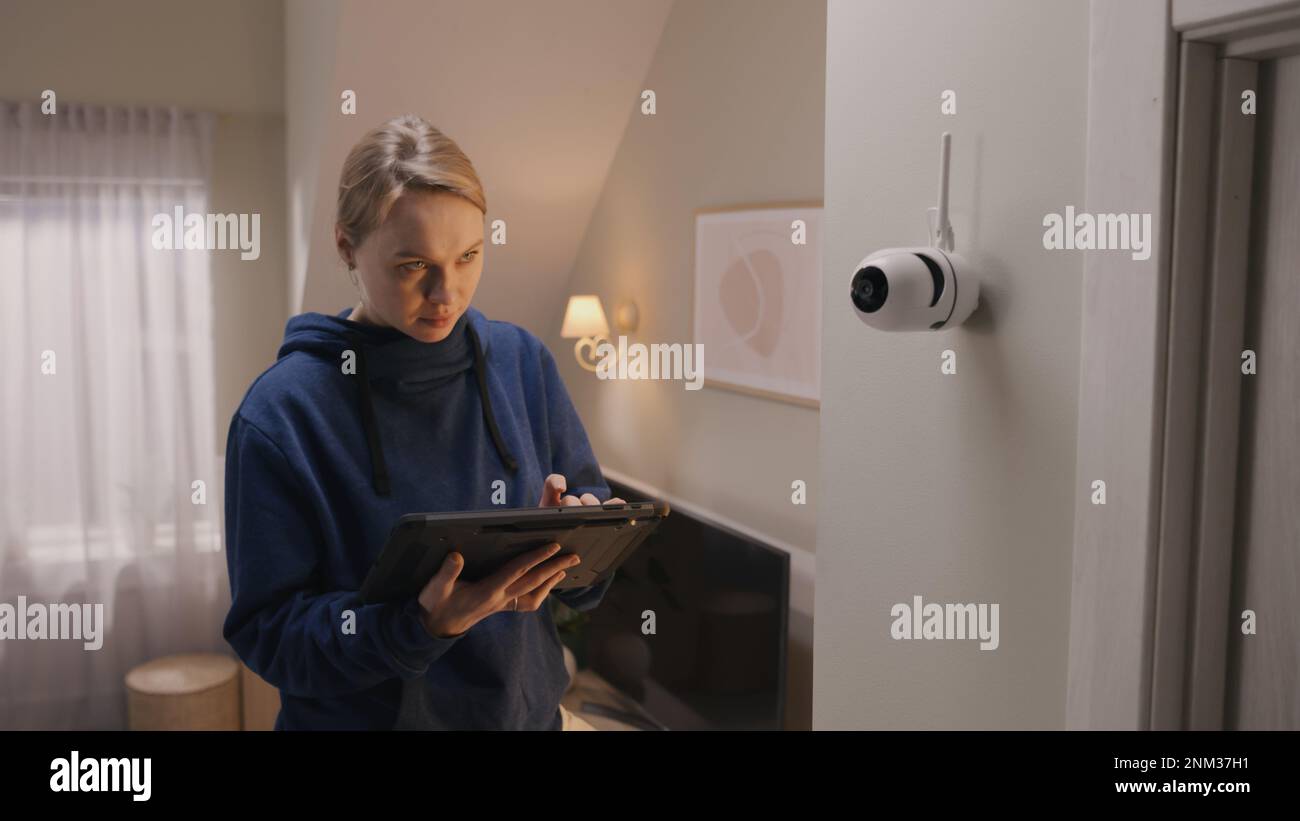 Caucasian woman installs security camera. Woman sets up angle of CCTV ...