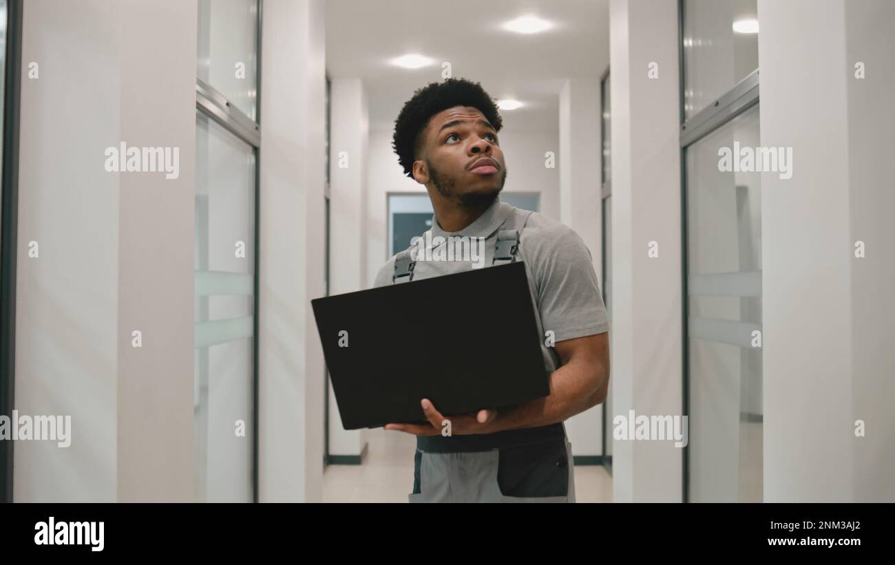 African American installer in uniform stands in corridor and sets up ...