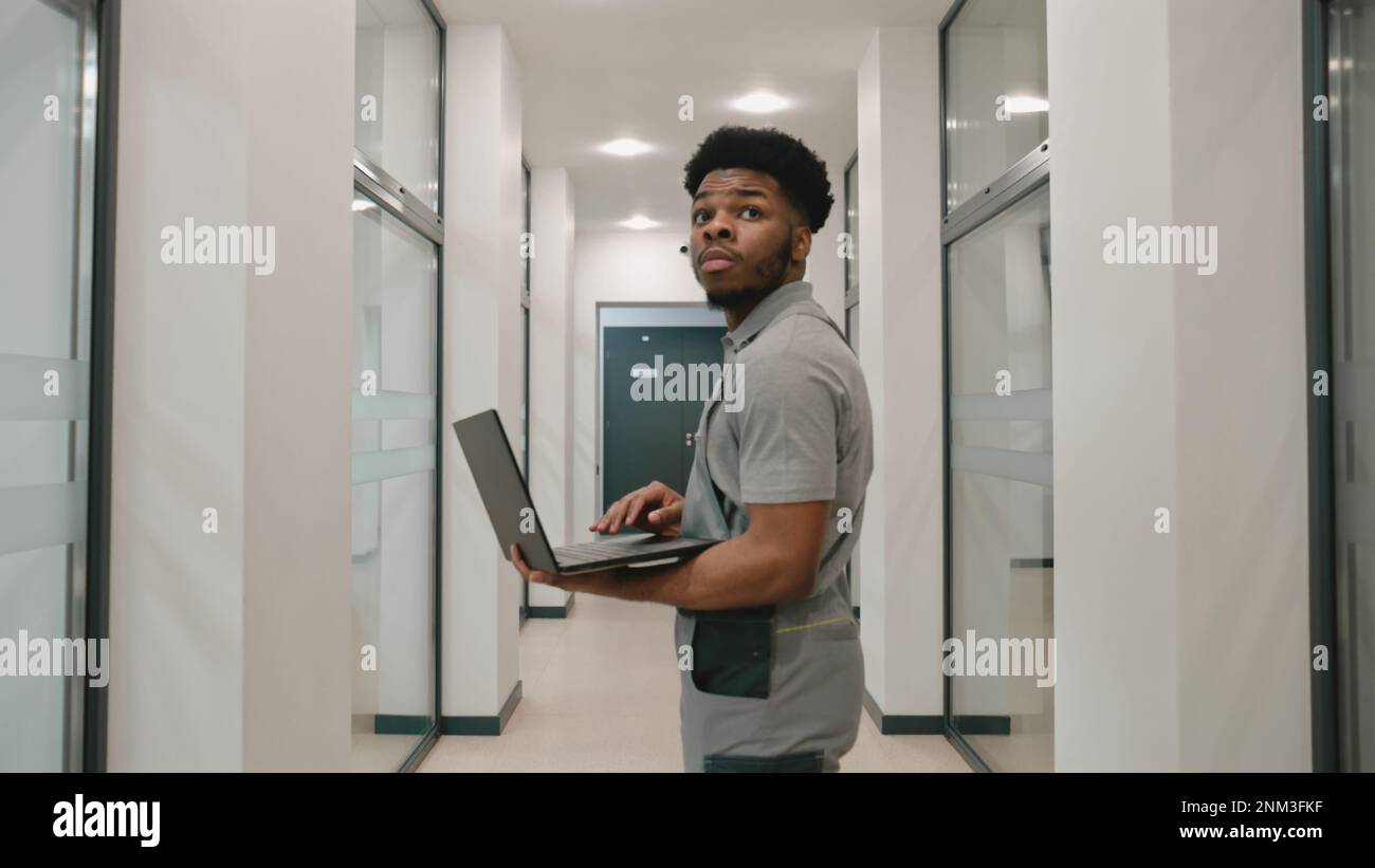 African American installer in uniform stands in hallway and sets up ...