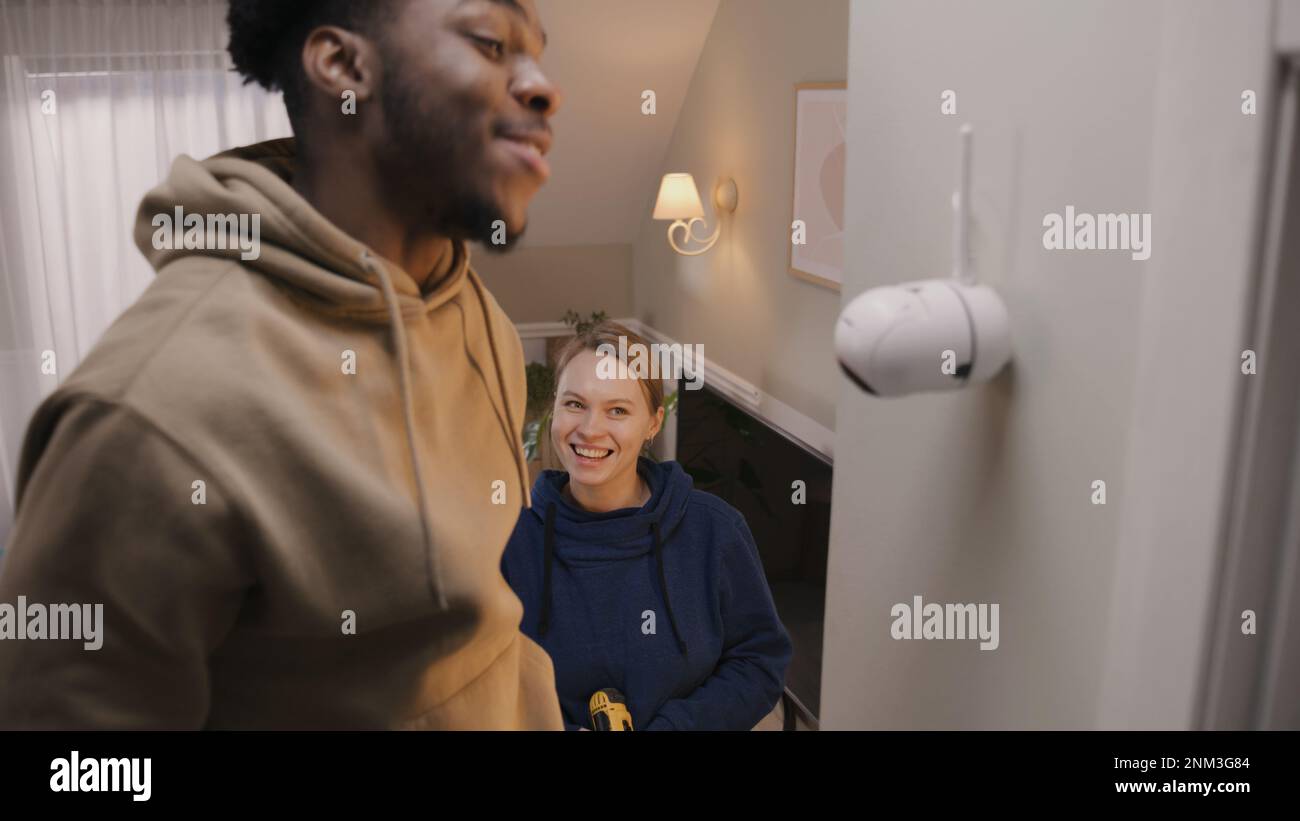 African American man connects security camera with wire and fastening ...
