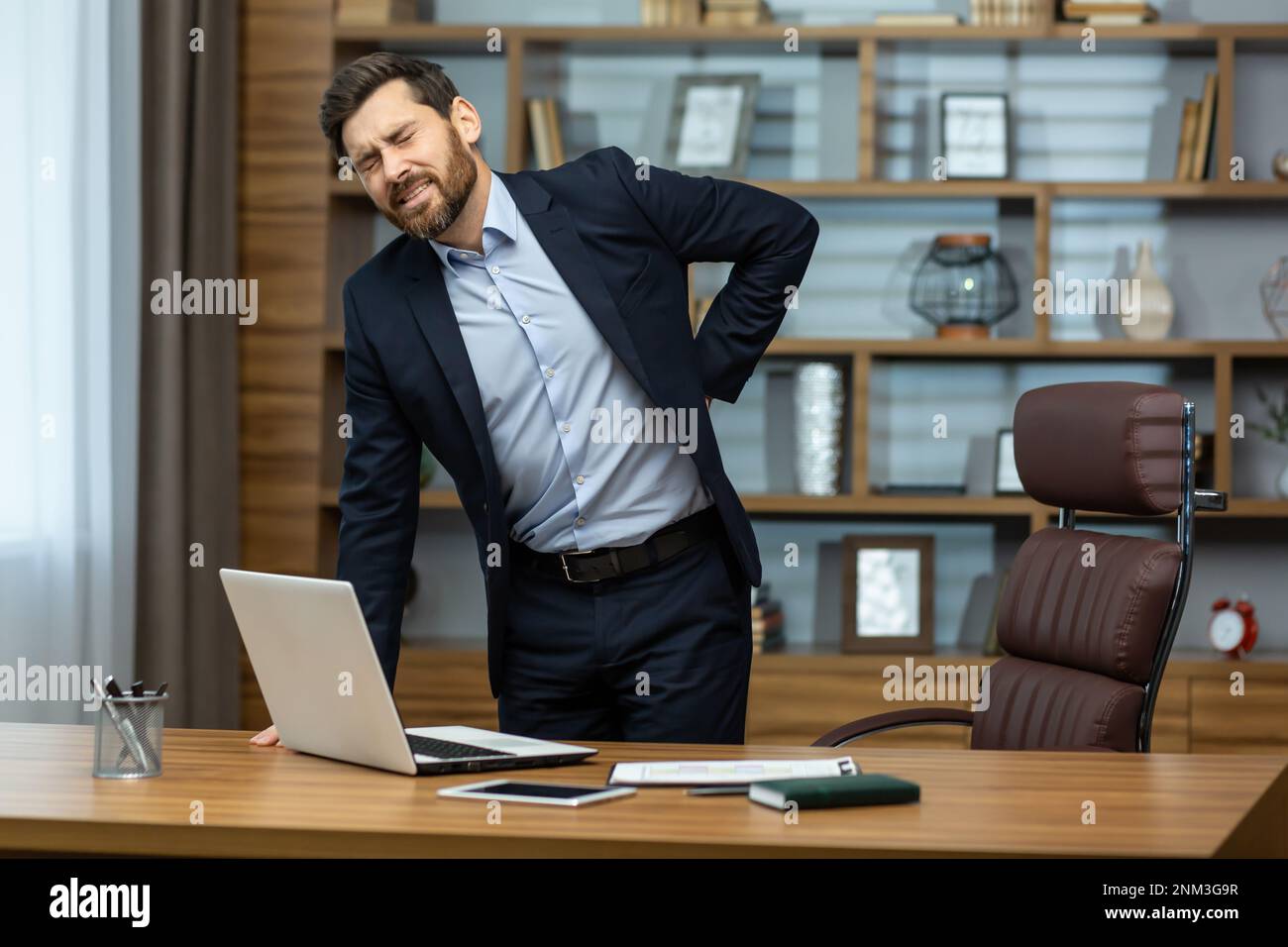 The problem of sedentary work. A young businessman man in a suit stands ...
