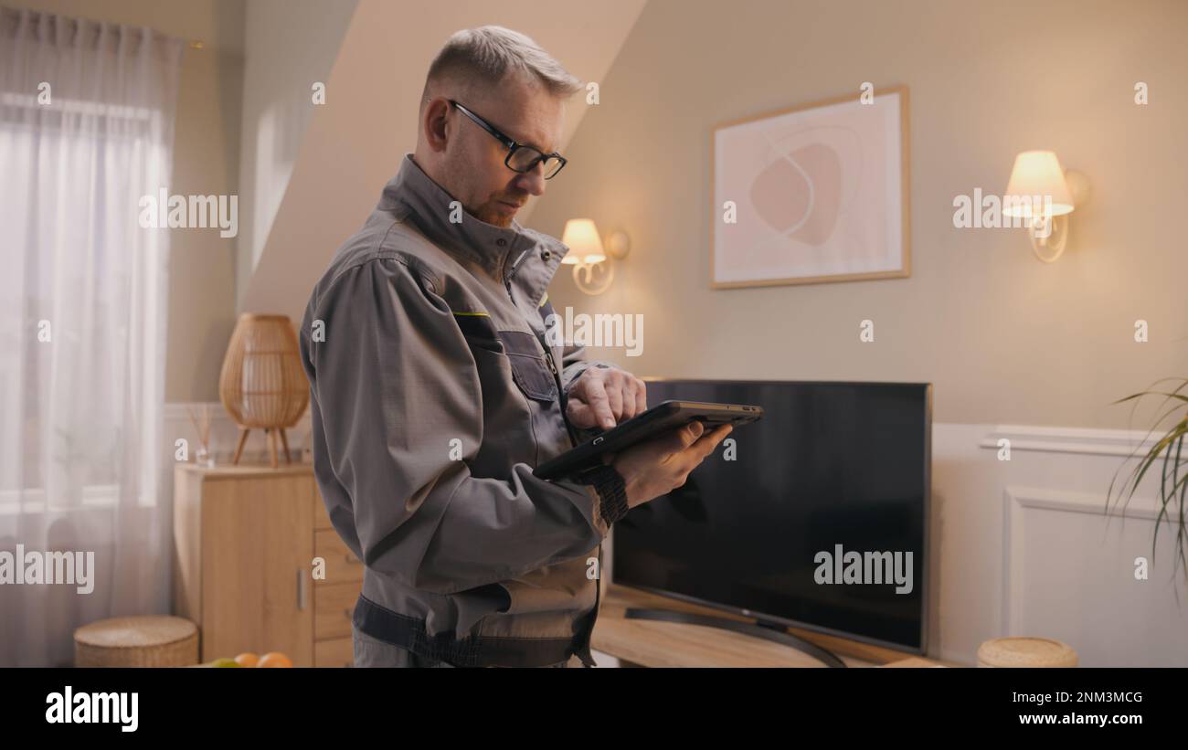 Male installer in uniform sets up security camera in apartment using ...