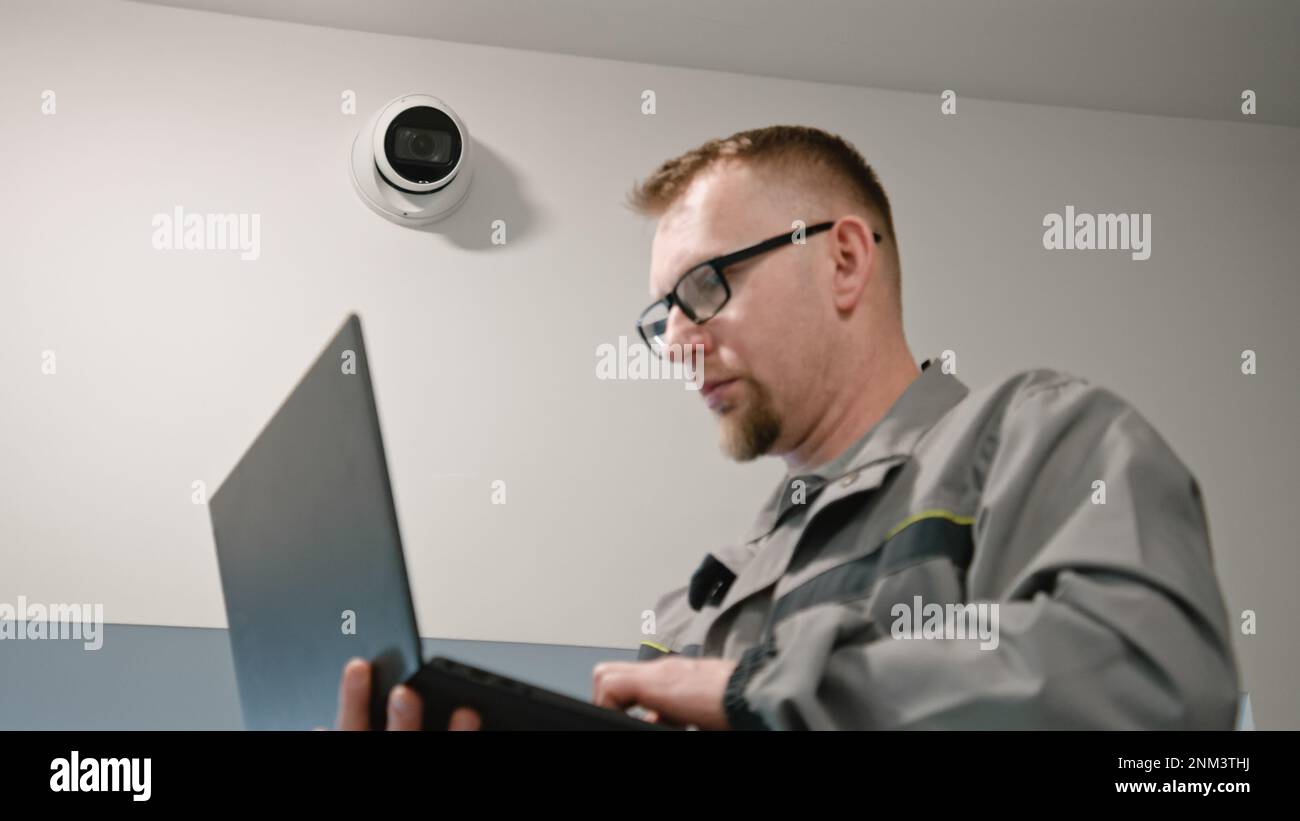 Installer in uniform sets up security camera in office room using ...