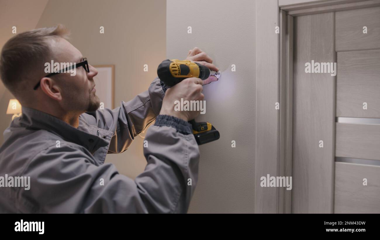 Man in uniform and glasses screws security camera mount into concrete ...