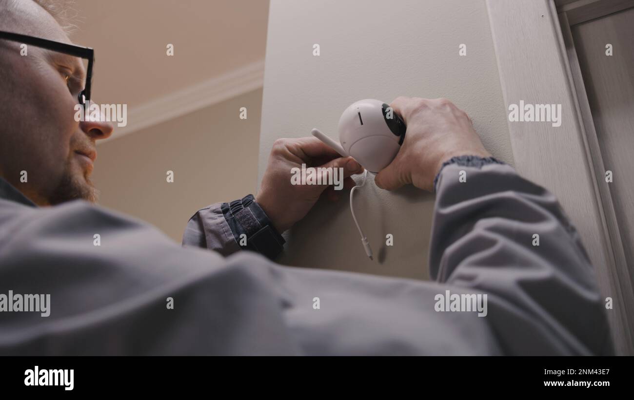 Installer in uniform puts security camera on wall fastening and ...