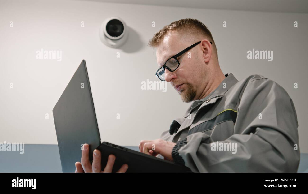 Installer in uniform sets up security camera in office room using ...