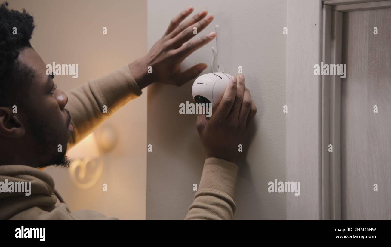 African American man puts security camera on wall fastening and ...