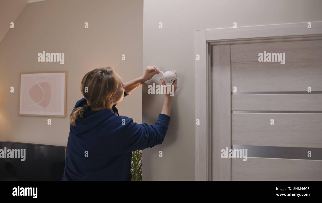 Woman puts security camera on wall mount, connects with cable. She ...